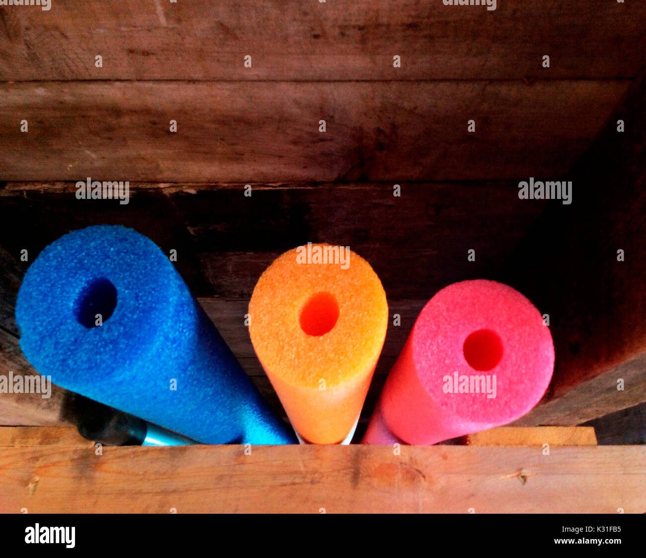 A trio of pool noodles in three different colours, stored on a shelf ...