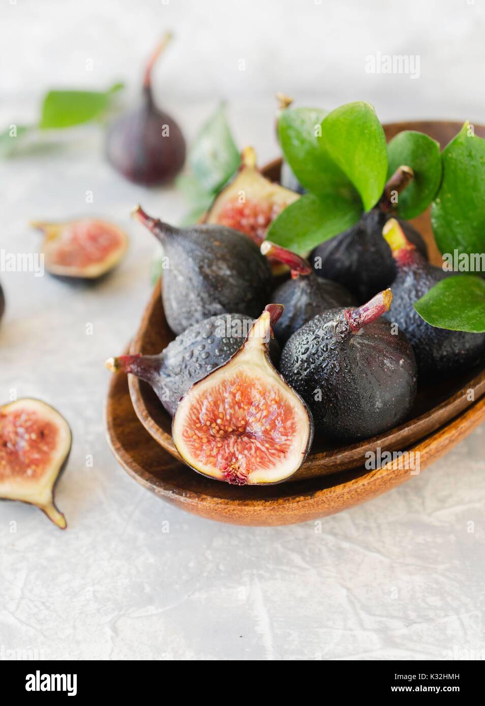 dark blue Fresh figs in a wooden bowl with greens on a white marble ...