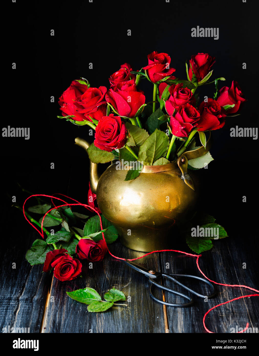 Bouquet of red roses in a copper jar with scissors on a black ...