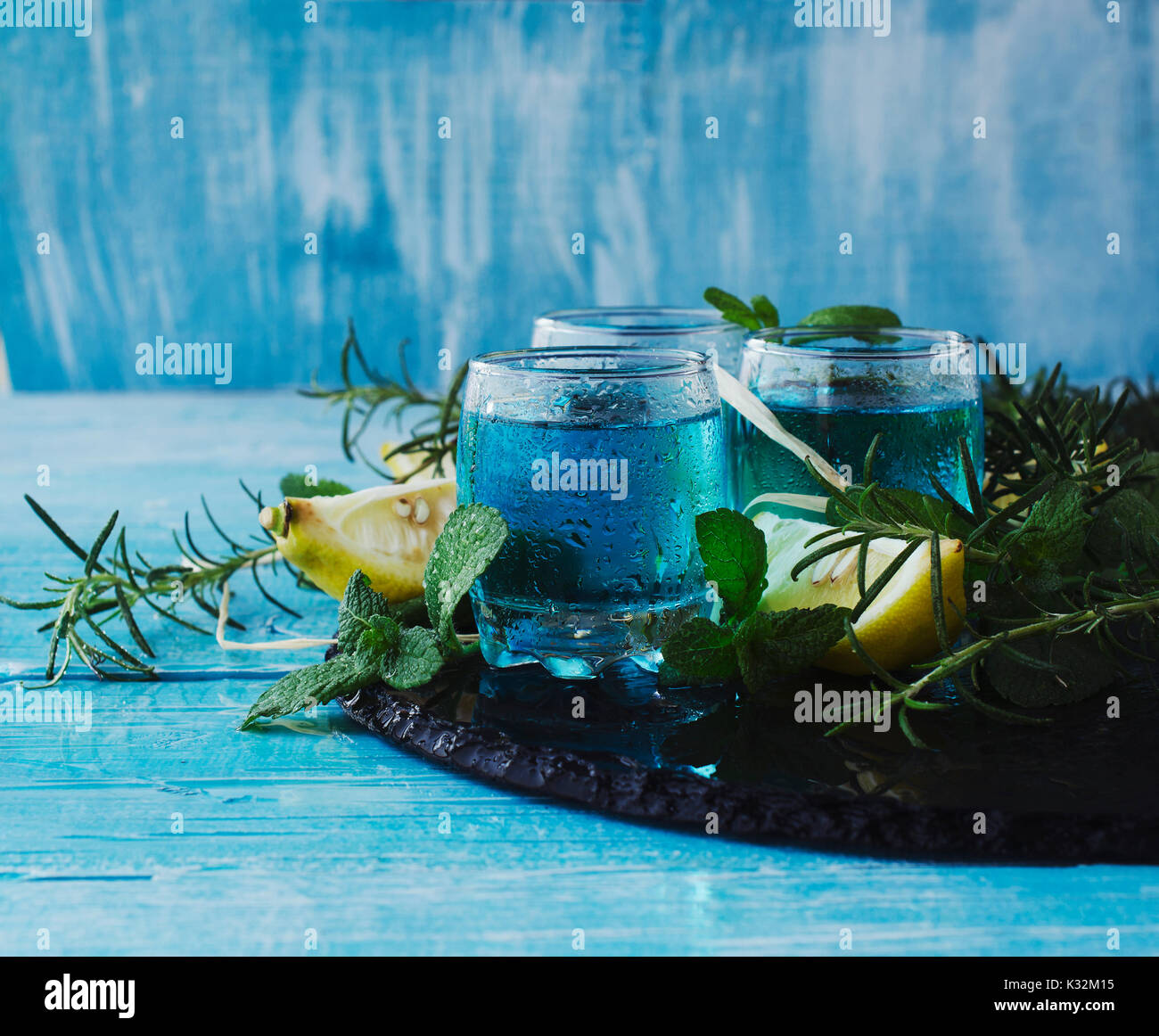 Blue curacao liqueur or sambuca with lemon on the wooden table ...