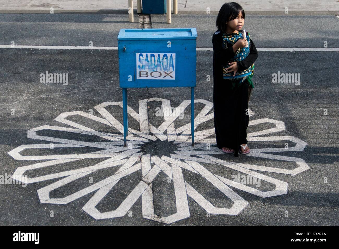 A young Muslim girl stands beside a Sadaqa box infront of the Blue ...