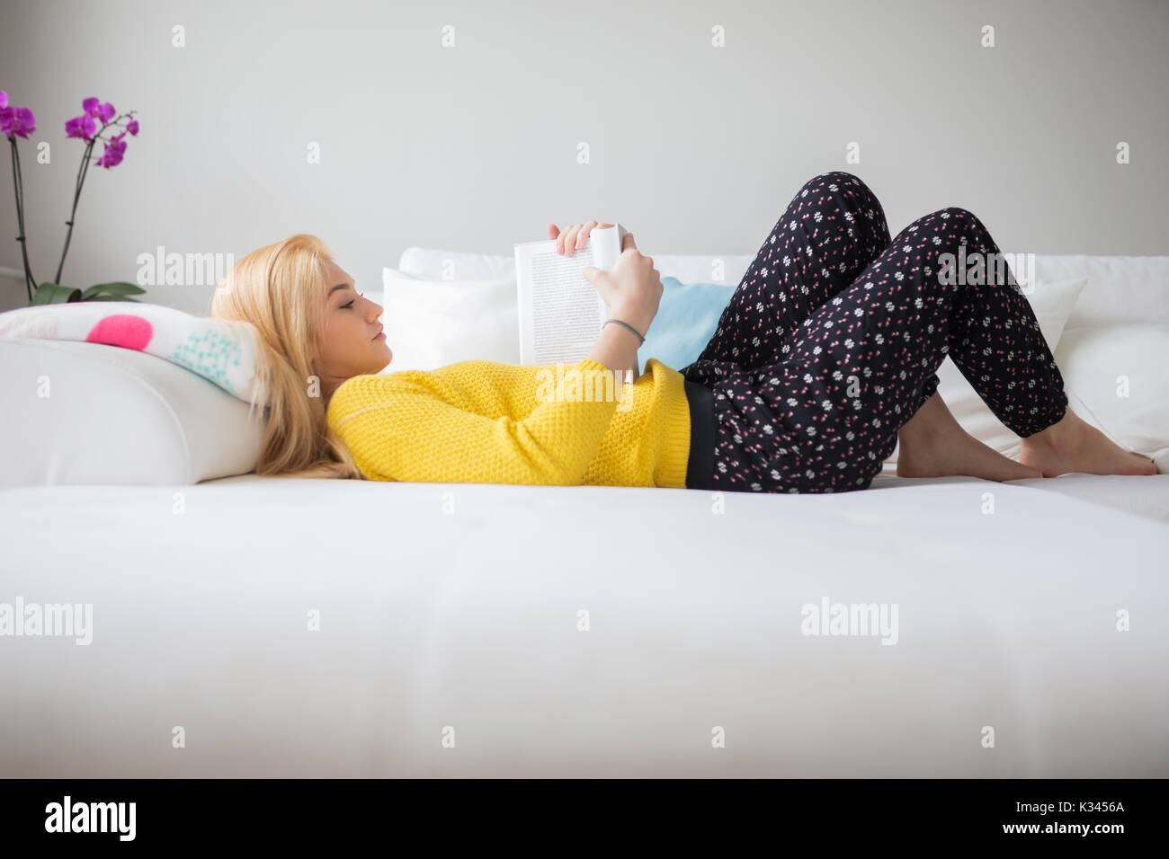 A photo of young woman lying on the couch and reading book intently ...