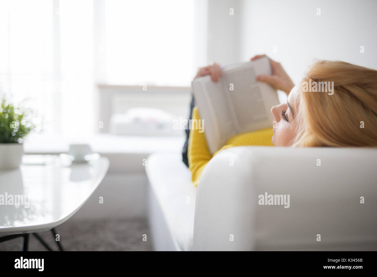 A photo of young, beautiful woman lying on the couch with book. She's ...