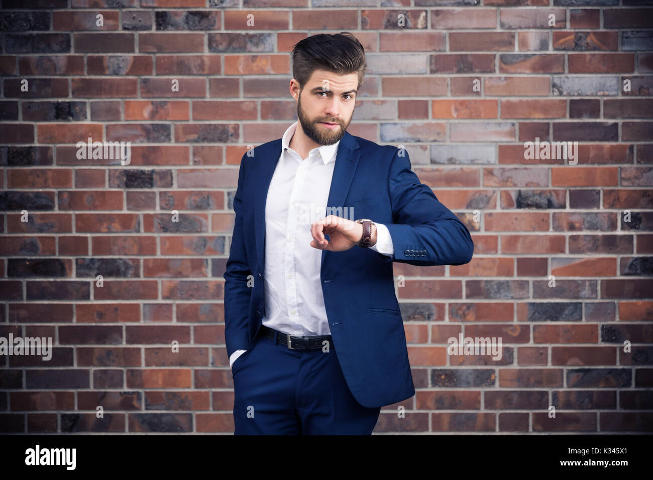 A photo of young man wearing navy suit. He's checking the time and ...