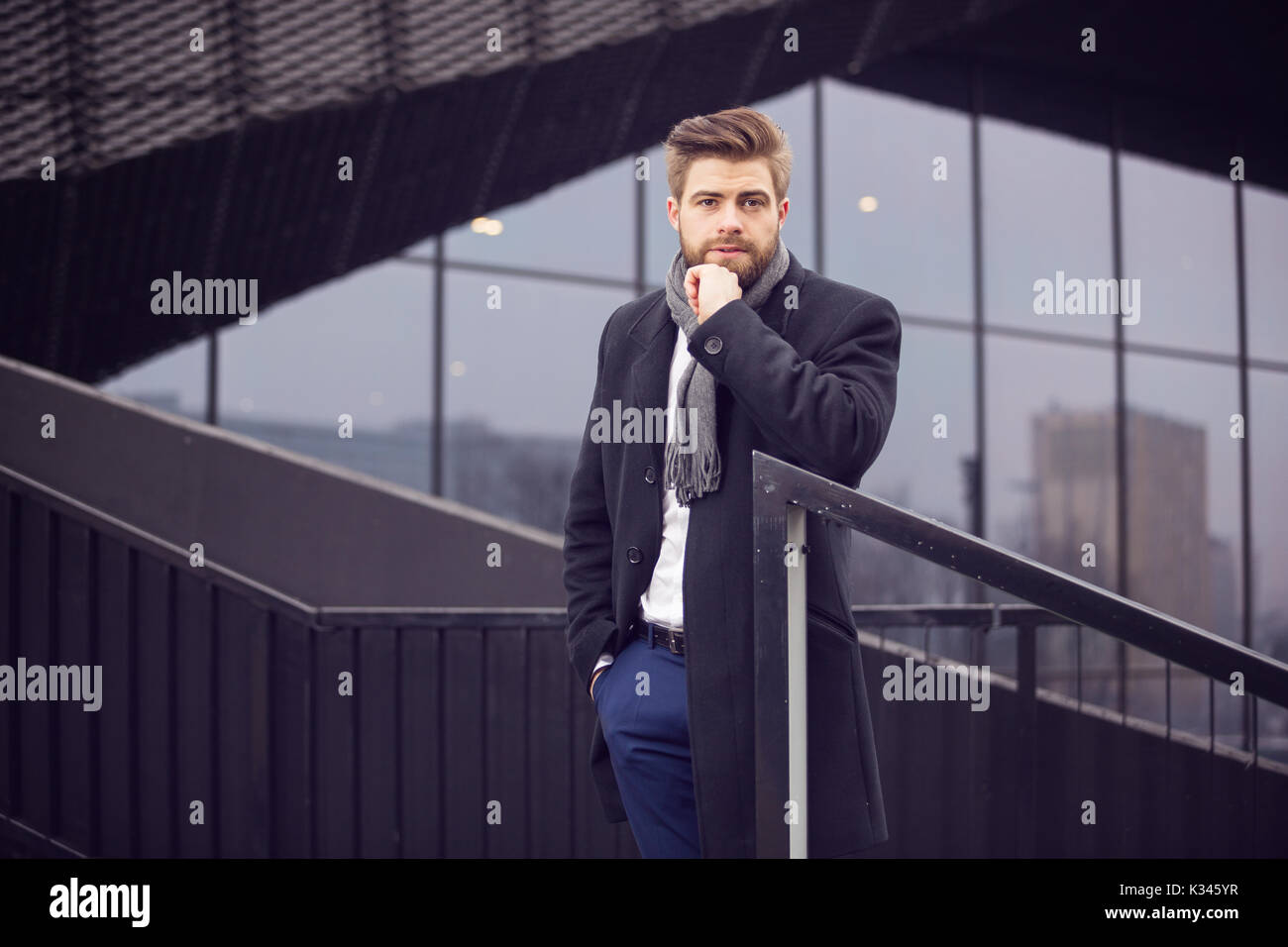 A photo of young, fashionable man leaning against rail and looking ...