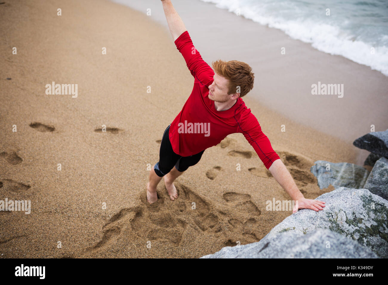 A photo of young man leaning against rock on the beach and stretching ...
