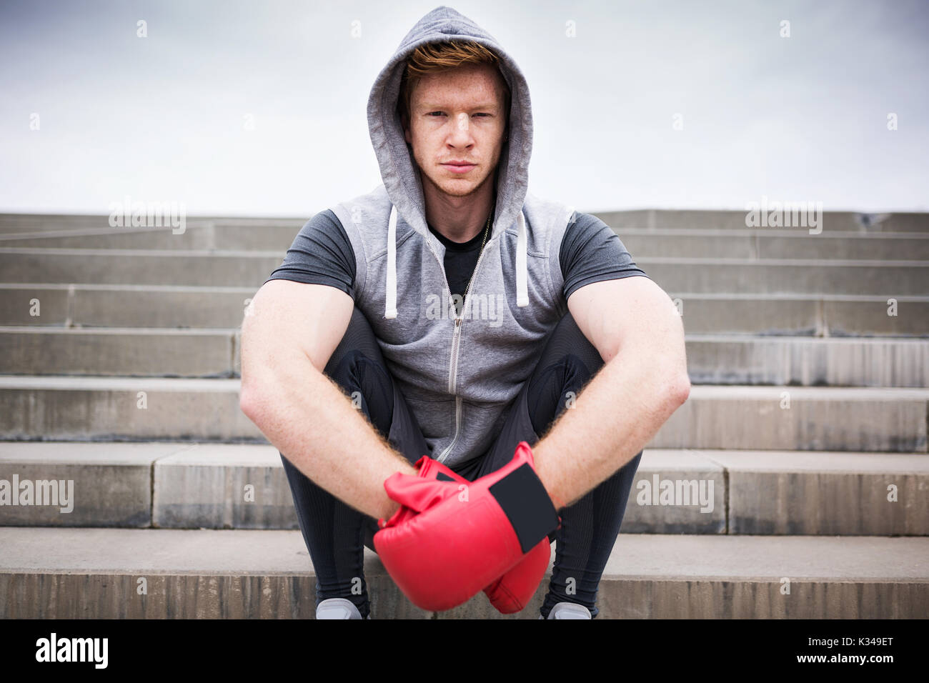A photo of young boxer sitting on the city stairs. He's wearing a hood ...