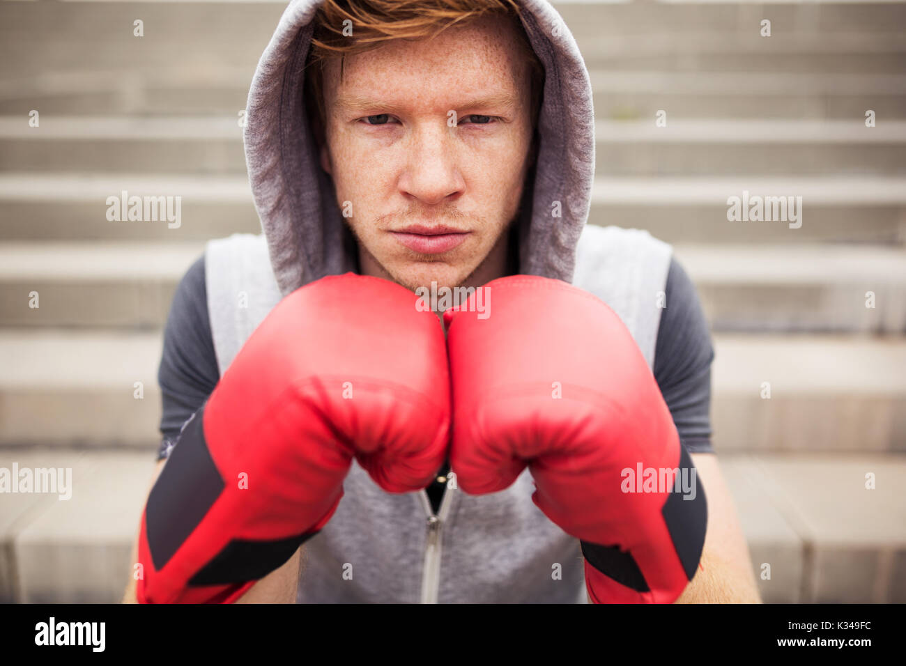 A photo of young boxer with red boxing gloves on his hands, a hood on ...