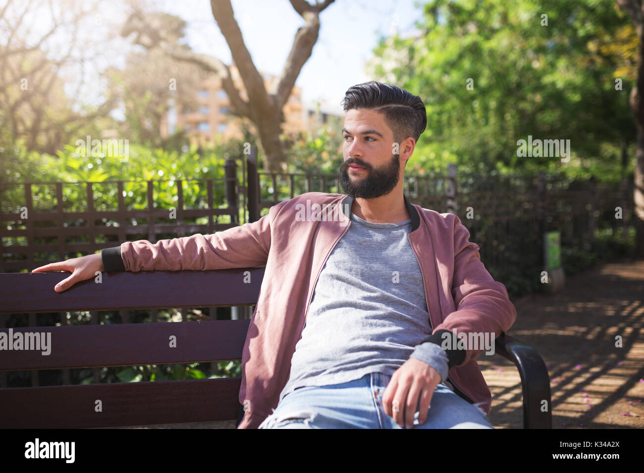 A photo of young man sitting on the bench in the park and waiting for ...