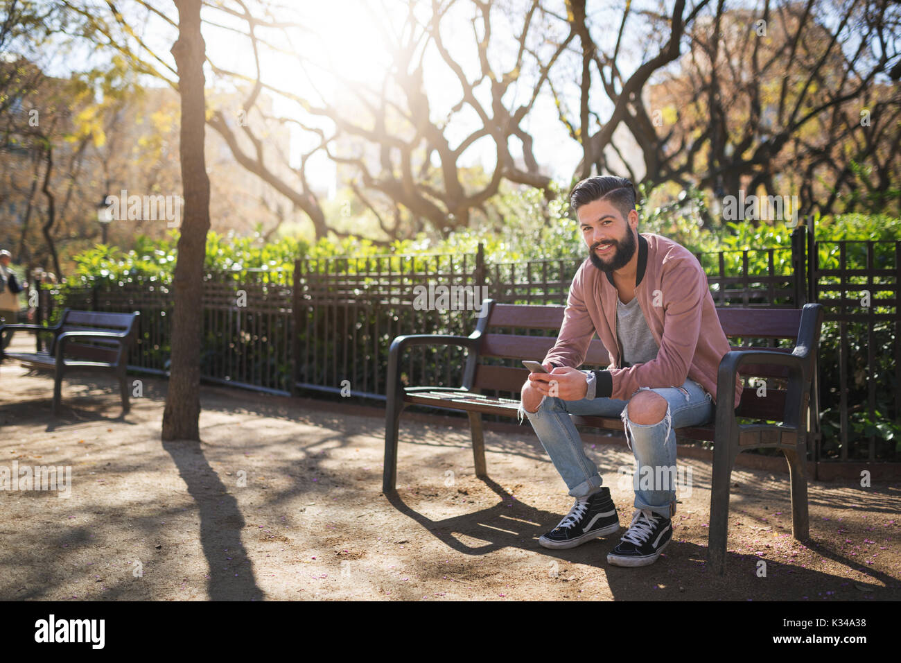 A photo of young man sitting on the bench in the park and texting his ...
