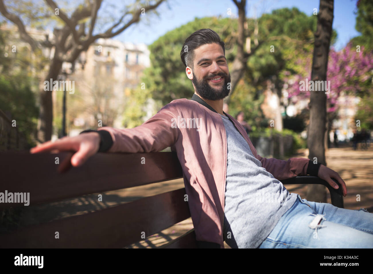 A photo of young man sitting on the park bench and smiling happily. He ...