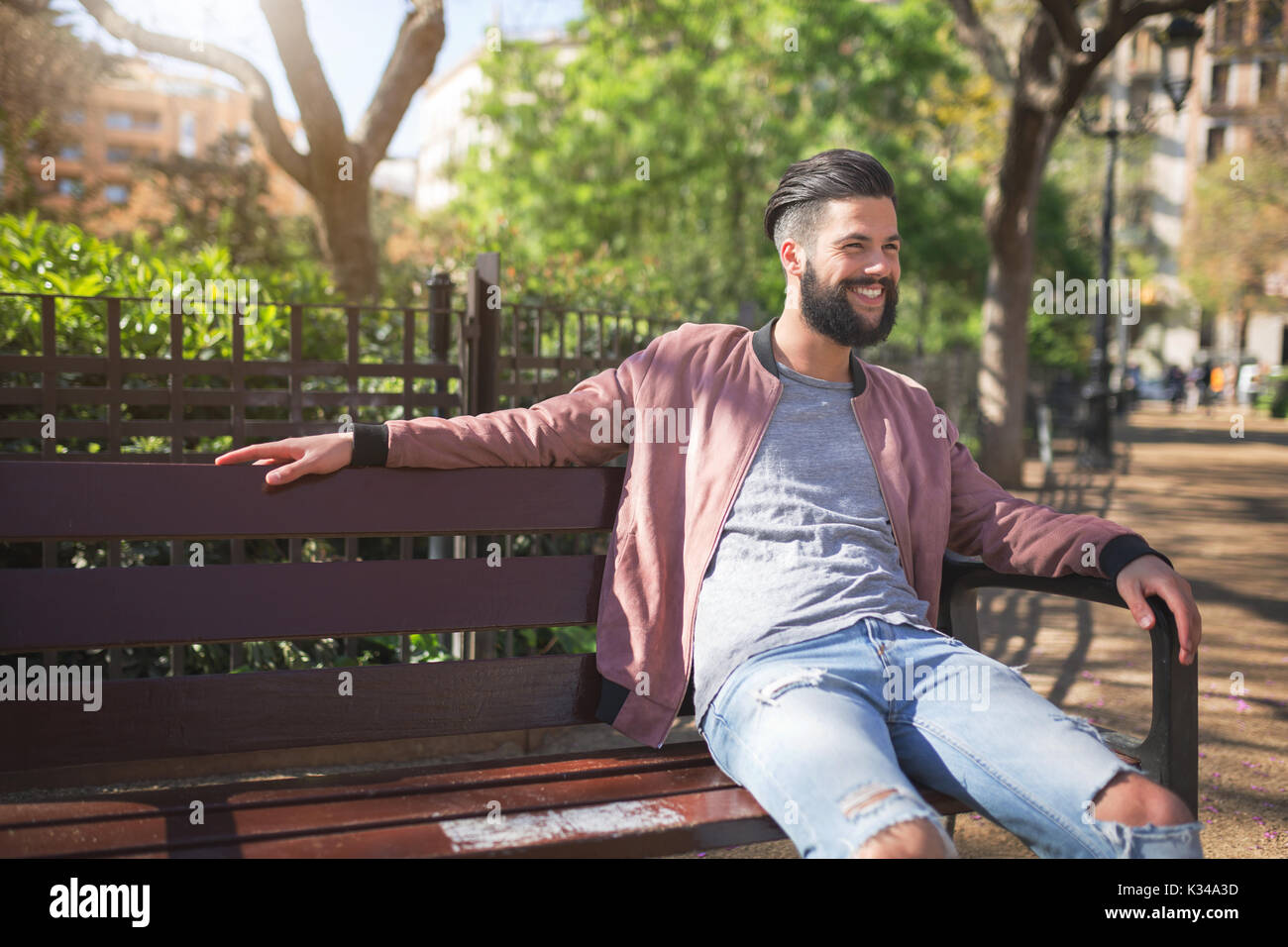A photo of young man sitting on the bench in the park and smiling ...