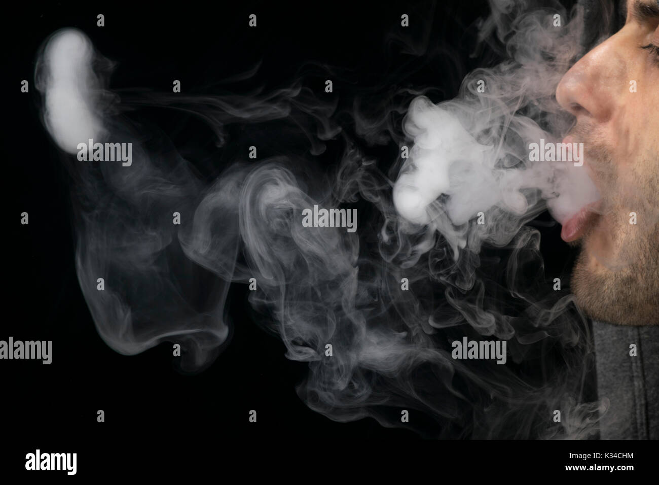 young man vaping electronic cigarette, holding a vape device with lots ...