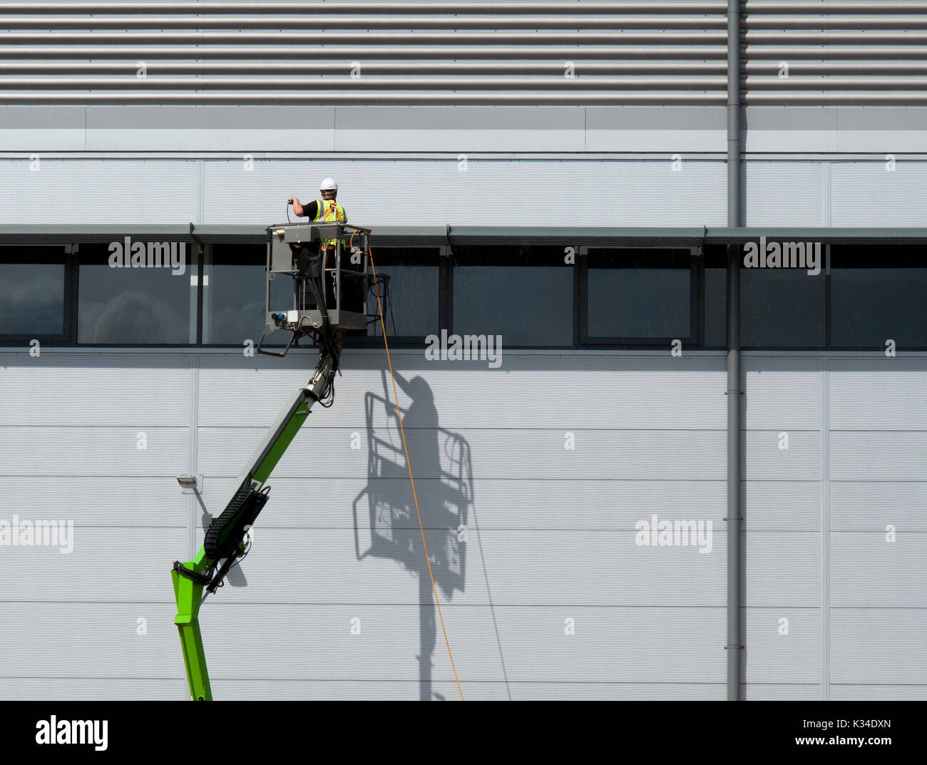 Construction worker on mobile boom lift cleaning external rainscreen ...