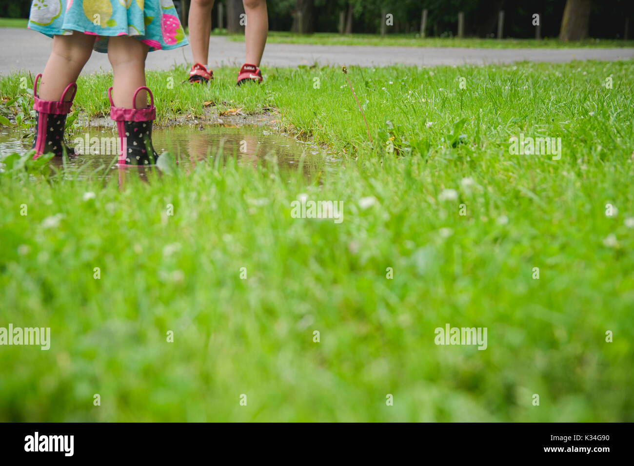 Children stand in a mud puddle wearing rain boots and with feet only ...