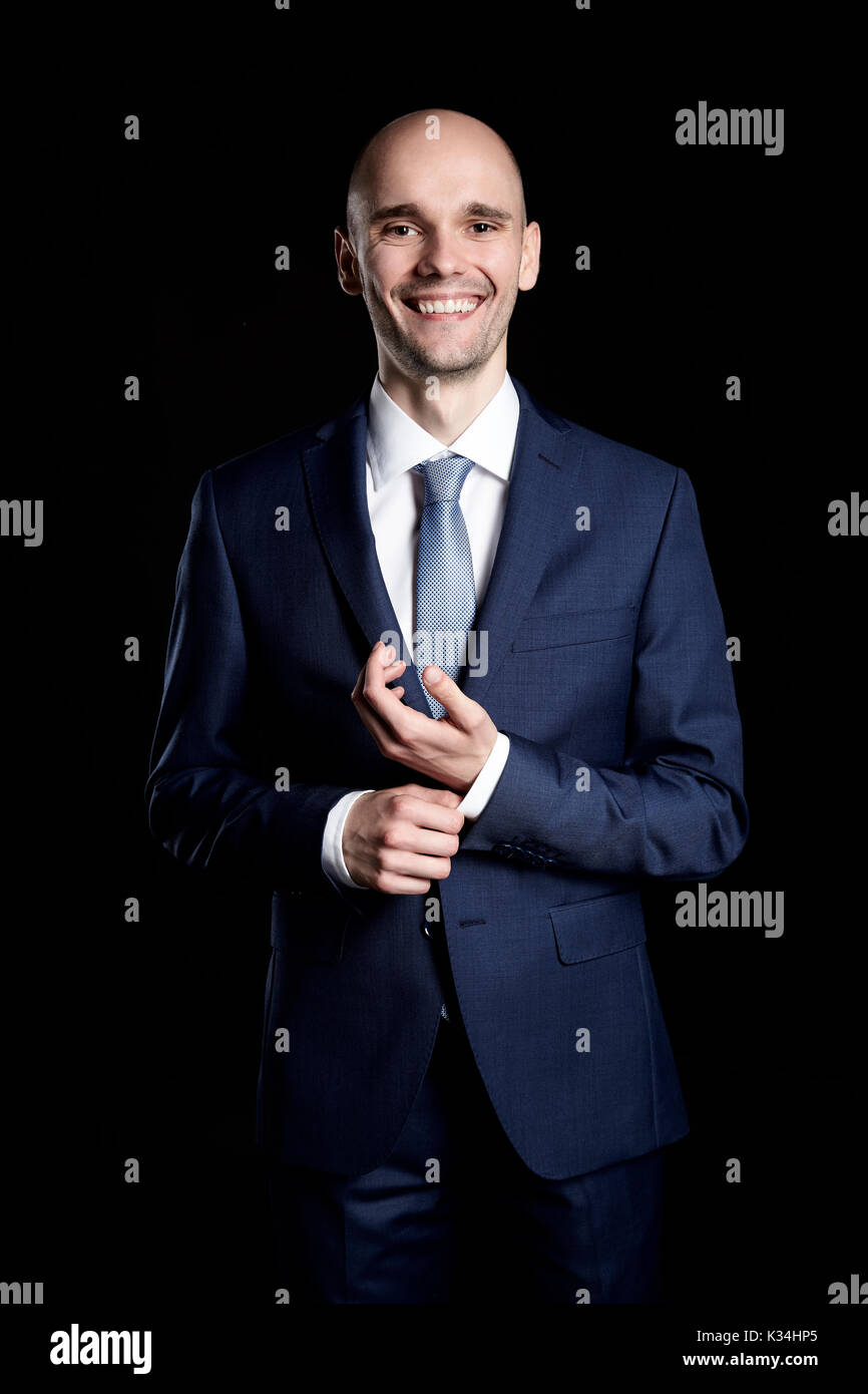 Smiling man fixing cuffs his suit. Studio shot of black background ...