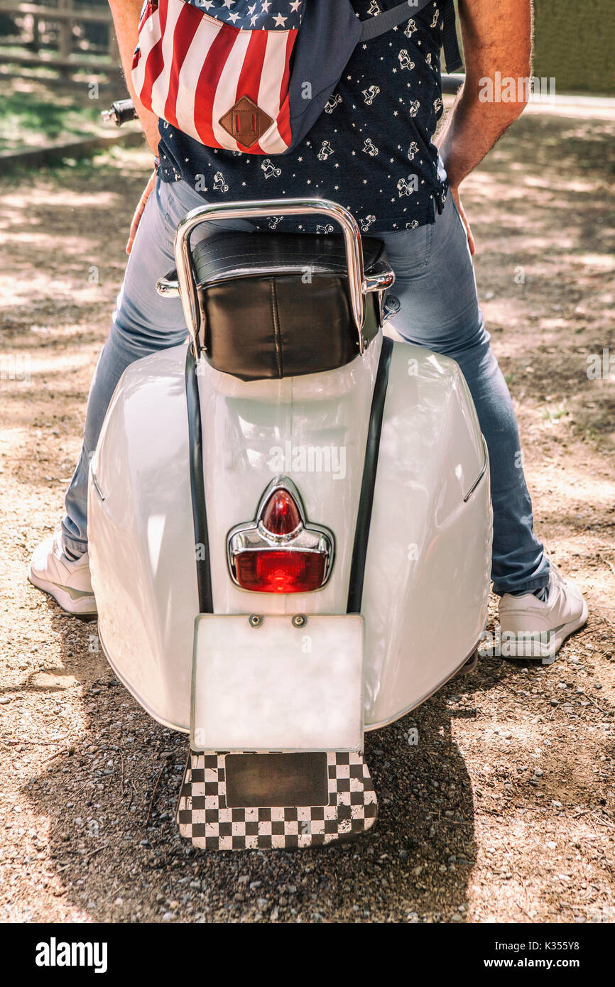 Stylish young man riding old style lambretta vespa through urban green ...