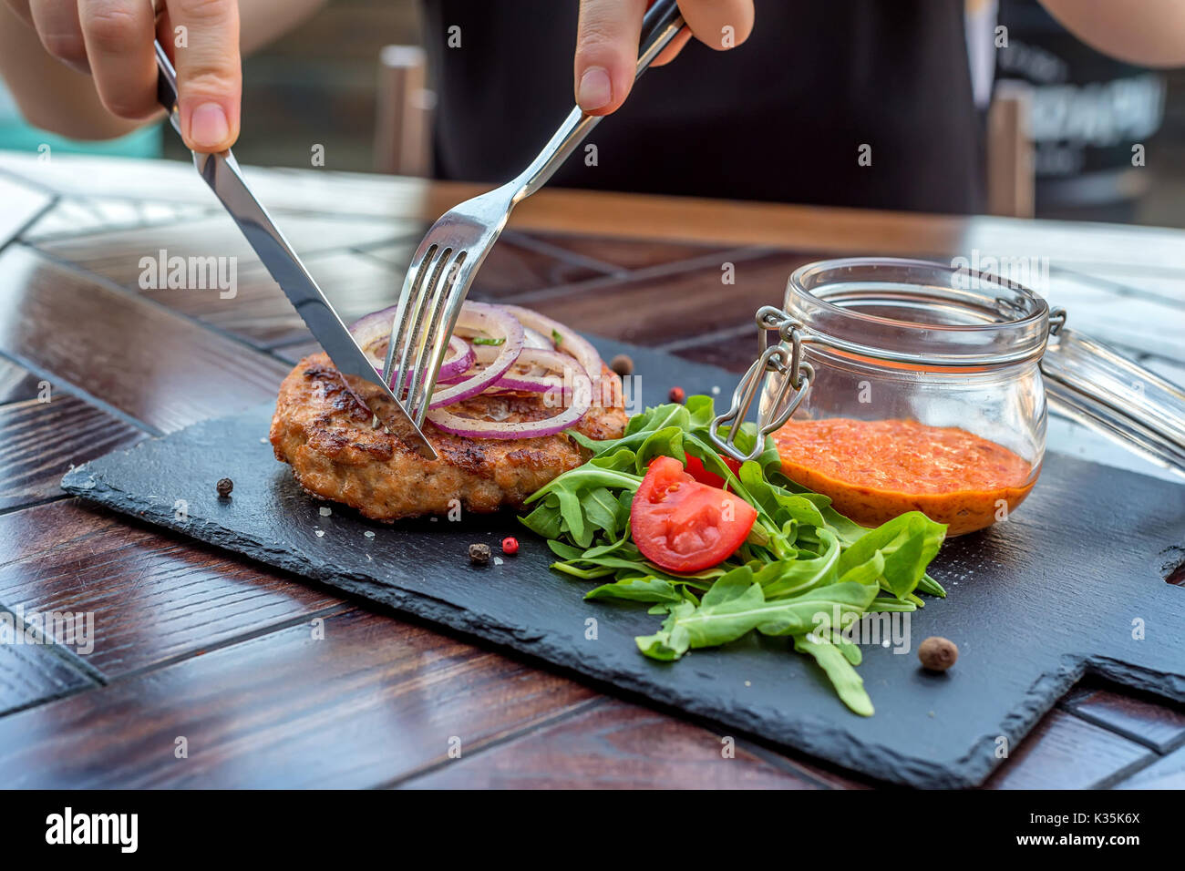 Close up female hands with knife and fork cutting grilled beef cutlet ...