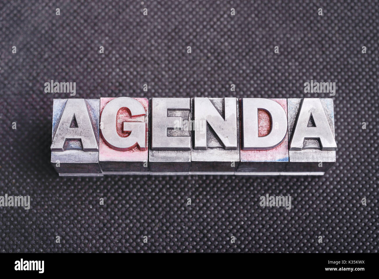 agenda word made from metallic letterpress blocks on black perforated ...