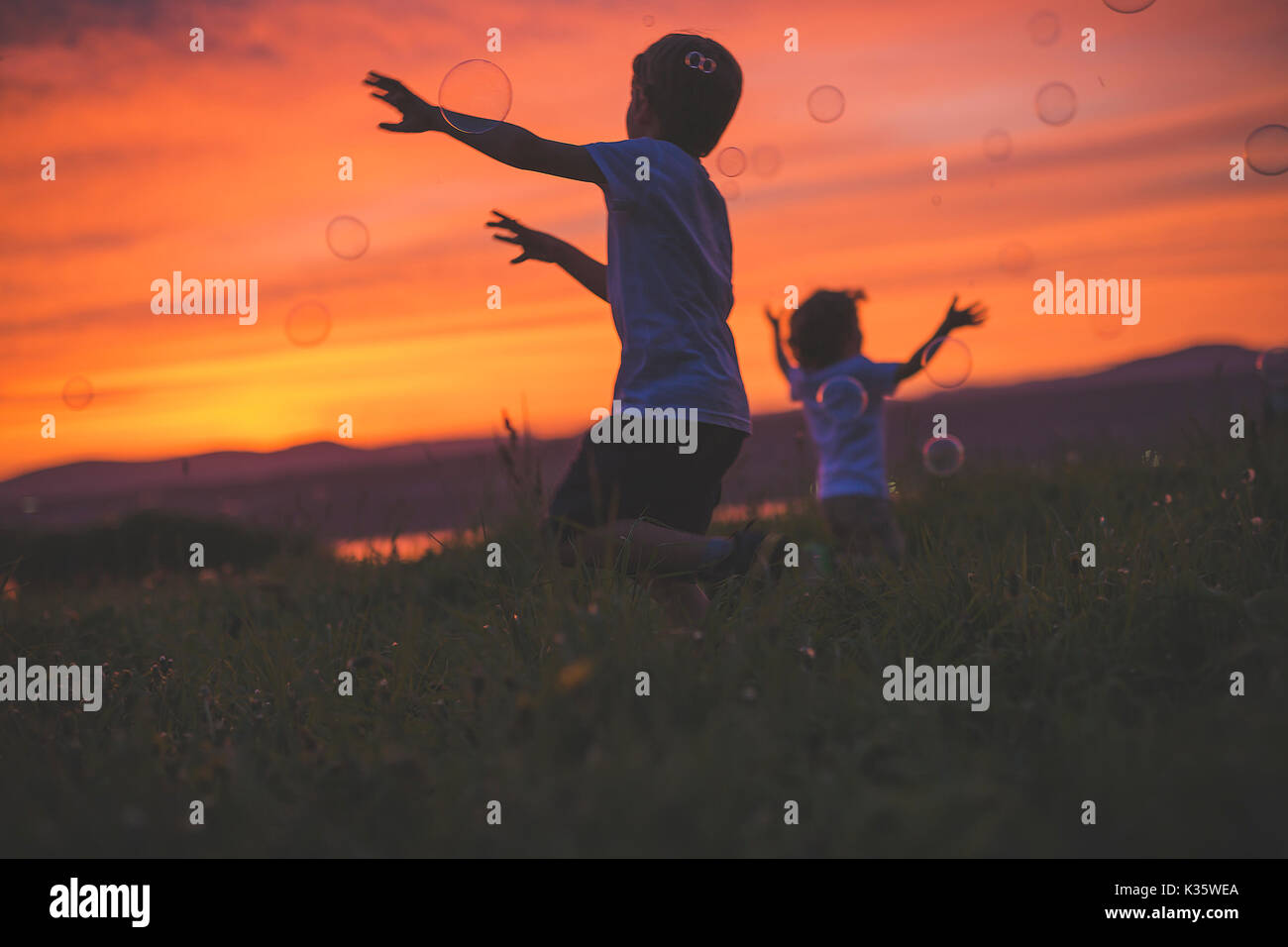 boys running to hit bubble on a sunset meadow Stock Photo - Alamy
