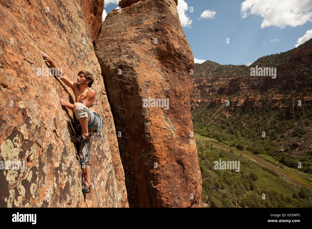 A young, male rock climber leading a route in a red rock canyon in the ...