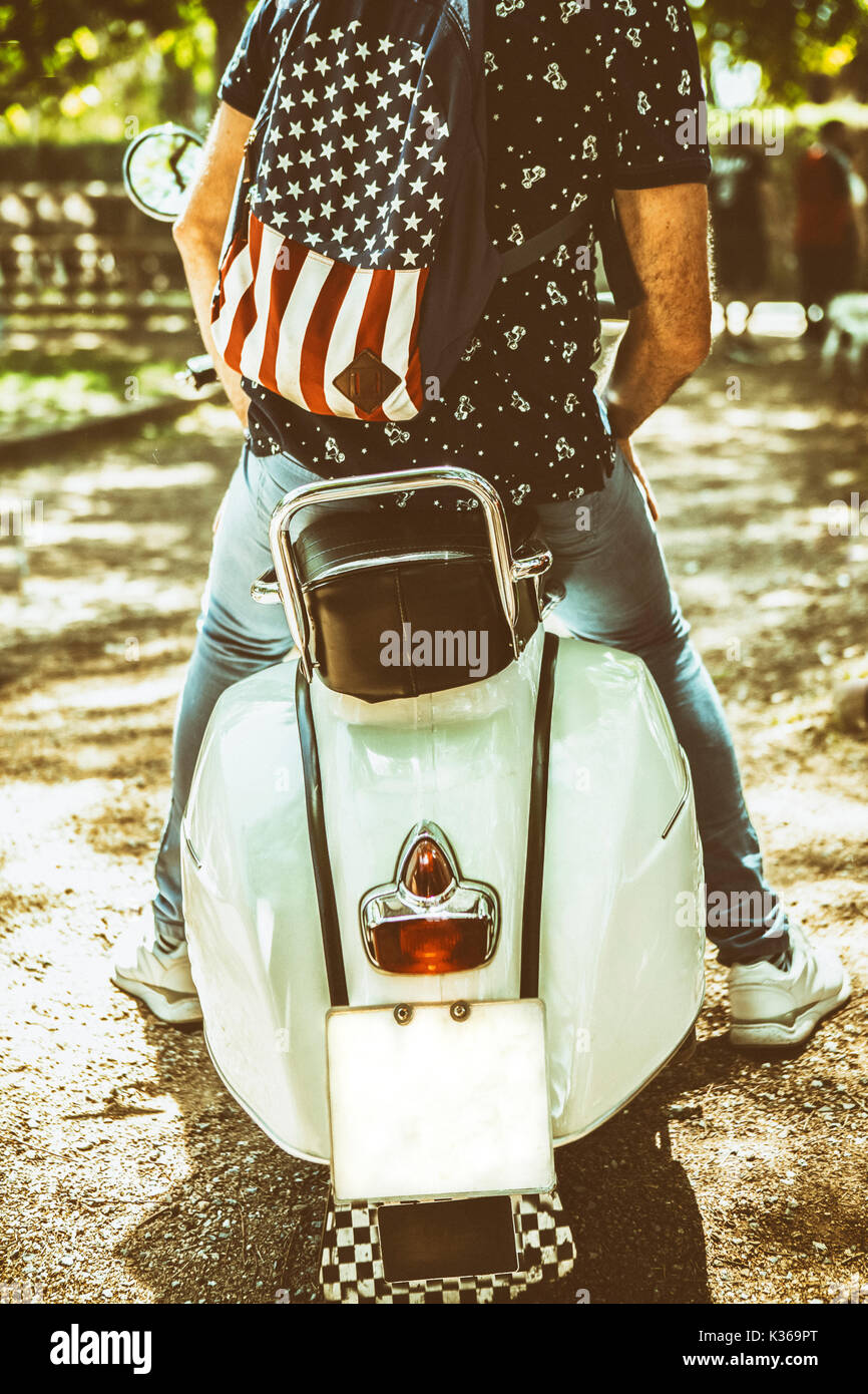 Stylish young man riding old style lambretta vespa through urban green ...