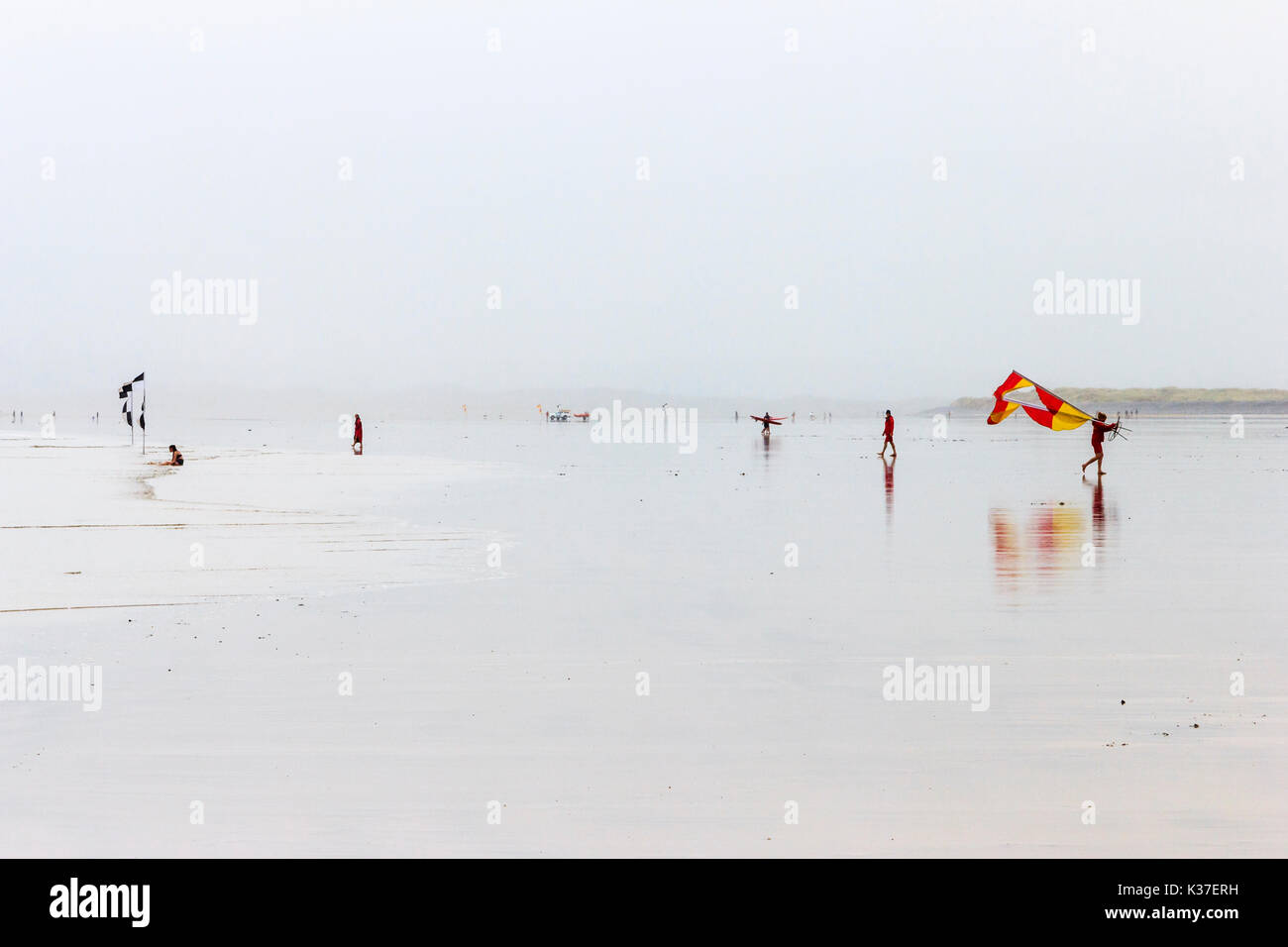 RNLI lifeguard carrying yellow and red warning flags and surfers on a ...