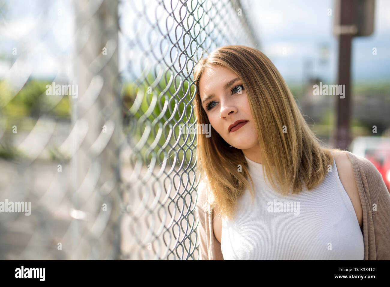 pretty young woman standing near chain link fence Stock Photo - Alamy