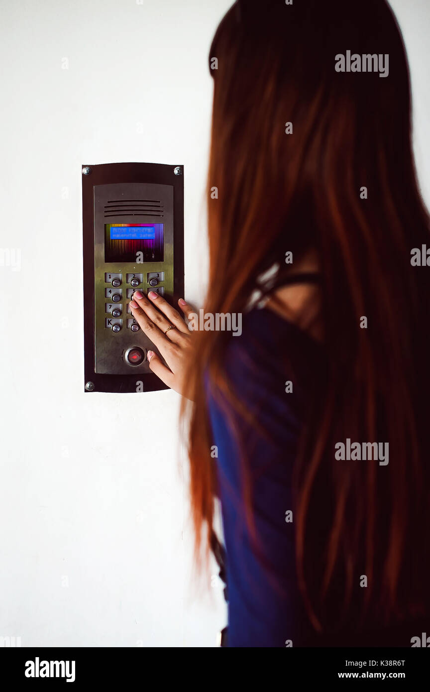 attractive woman in a blue elegant dress, dials code into intercom, at ...