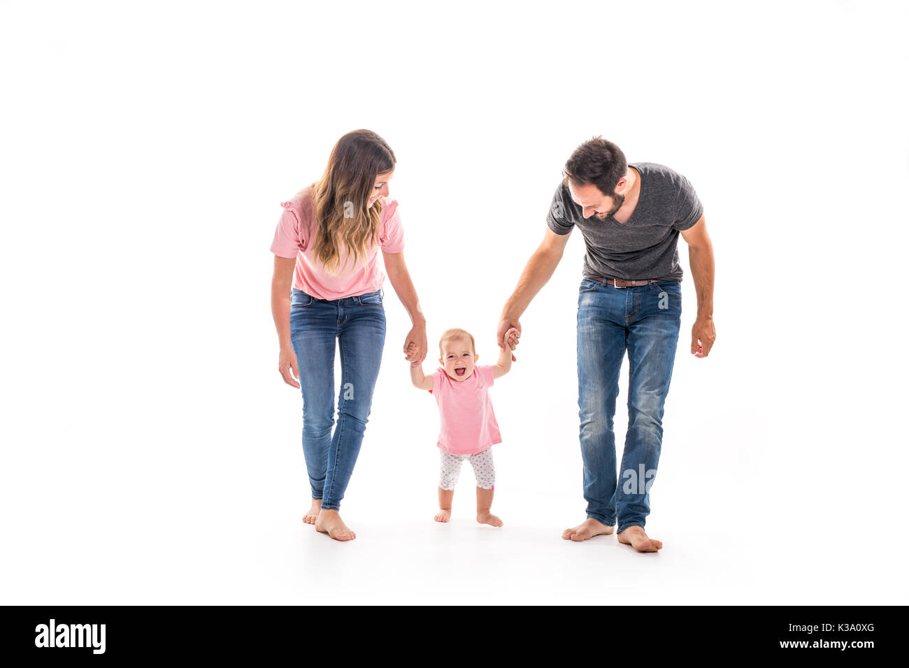 Couple of young parents helping their baby to make first steps on floor ...