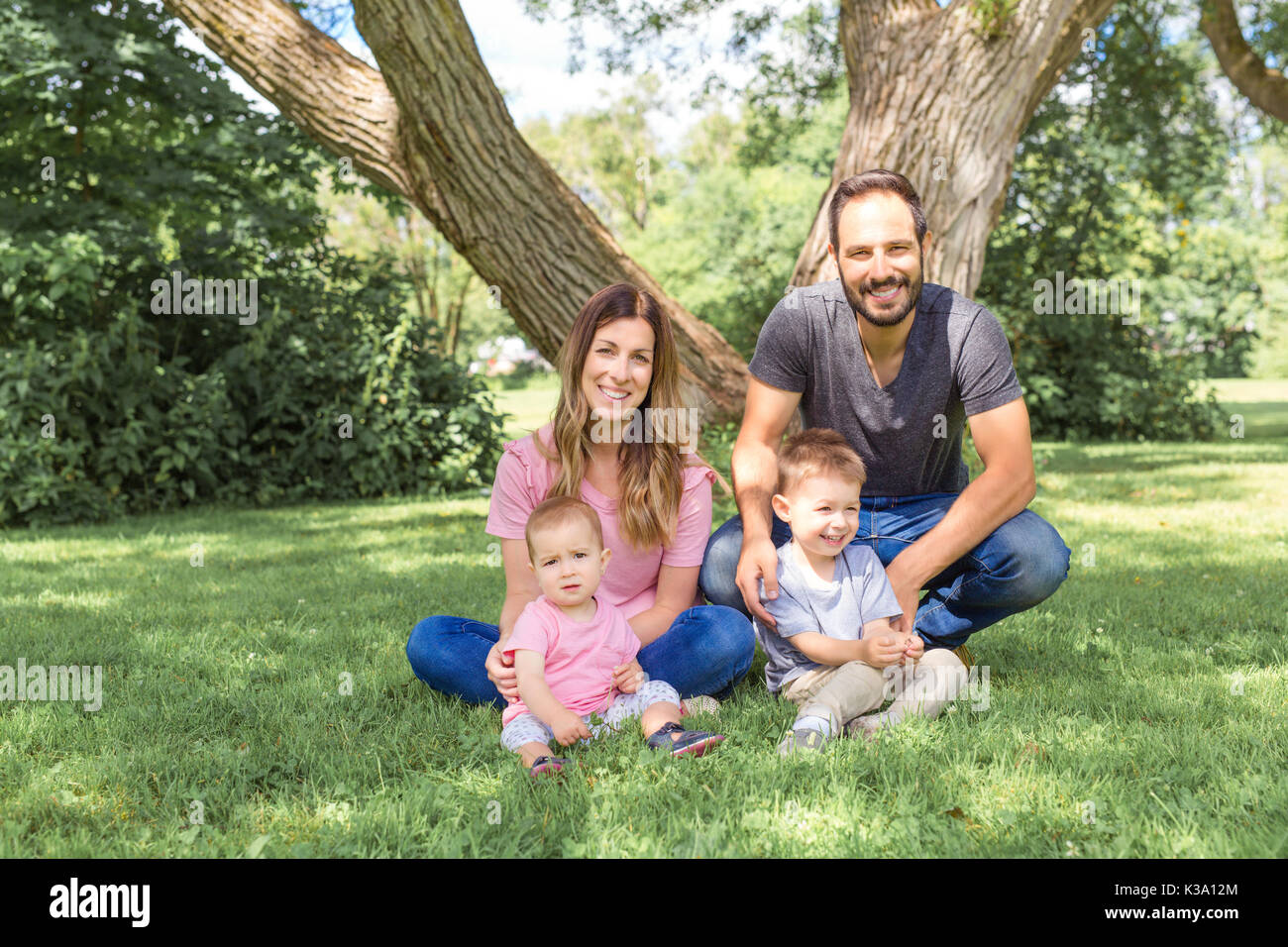 Parents Sitting With Children In Field close to a tree Stock Photo - Alamy