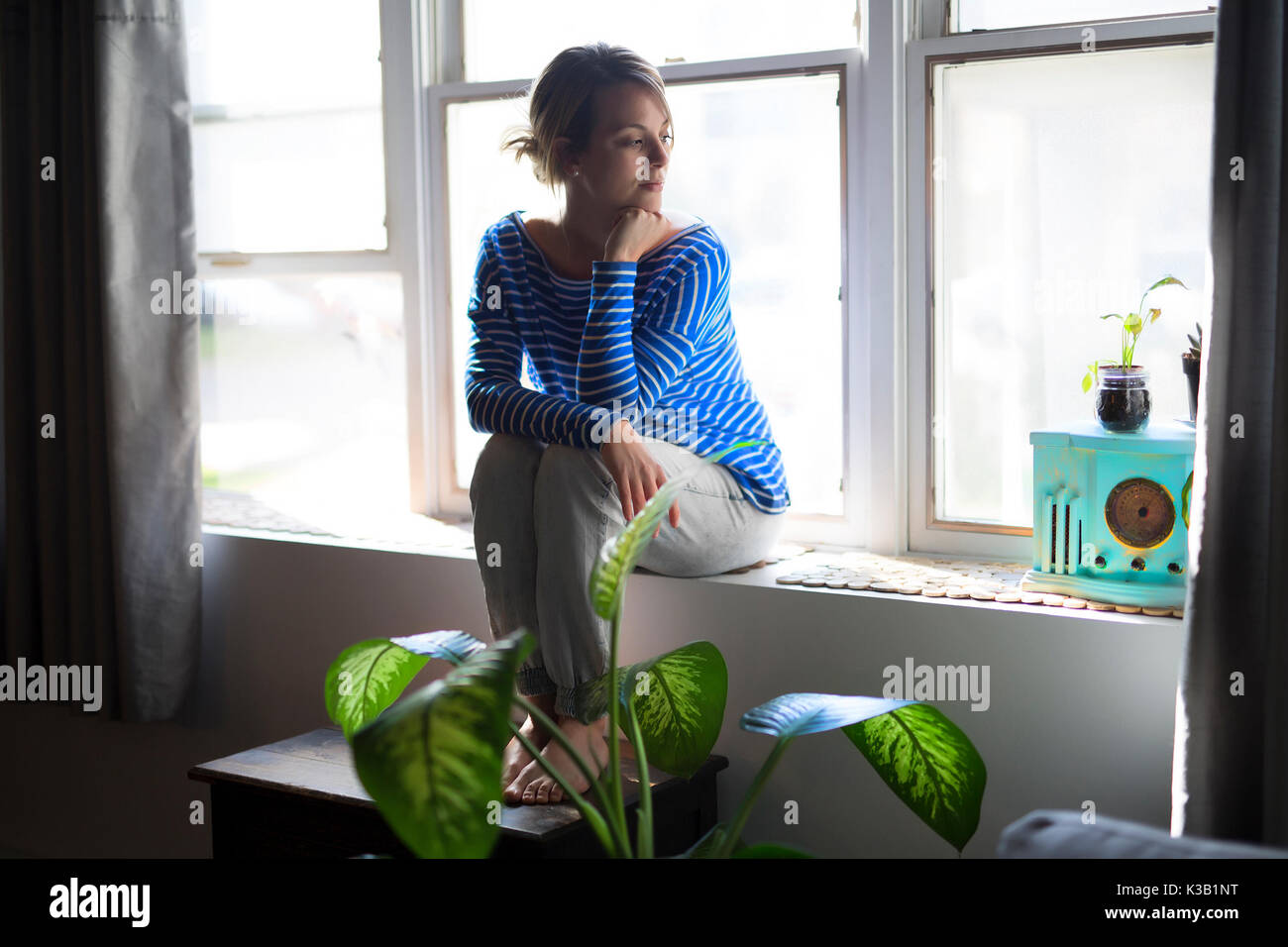 Beautiful young woman sitting near window Stock Photo - Alamy
