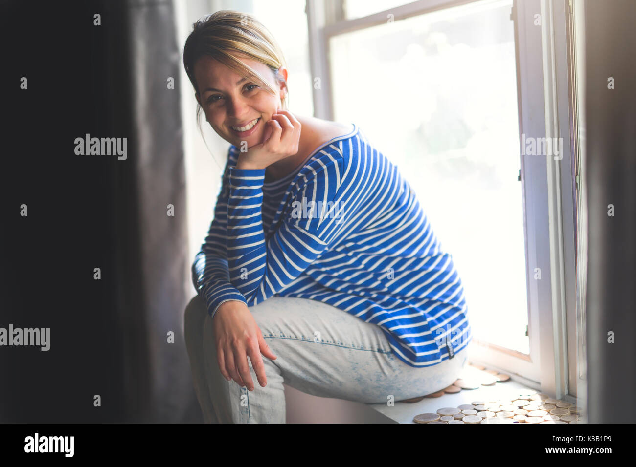 Beautiful young woman sitting near window Stock Photo - Alamy