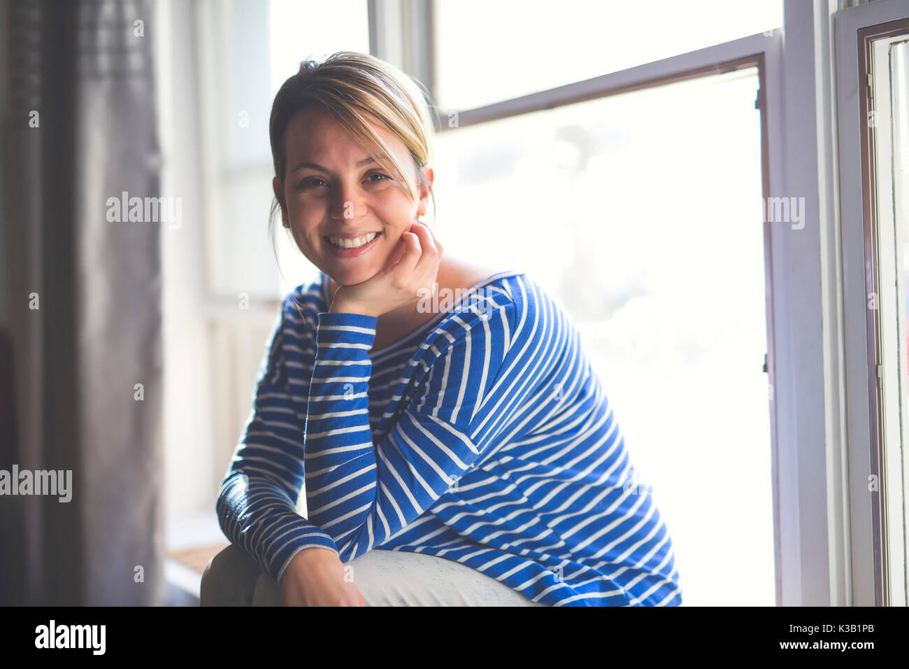 Beautiful young woman sitting near window Stock Photo - Alamy