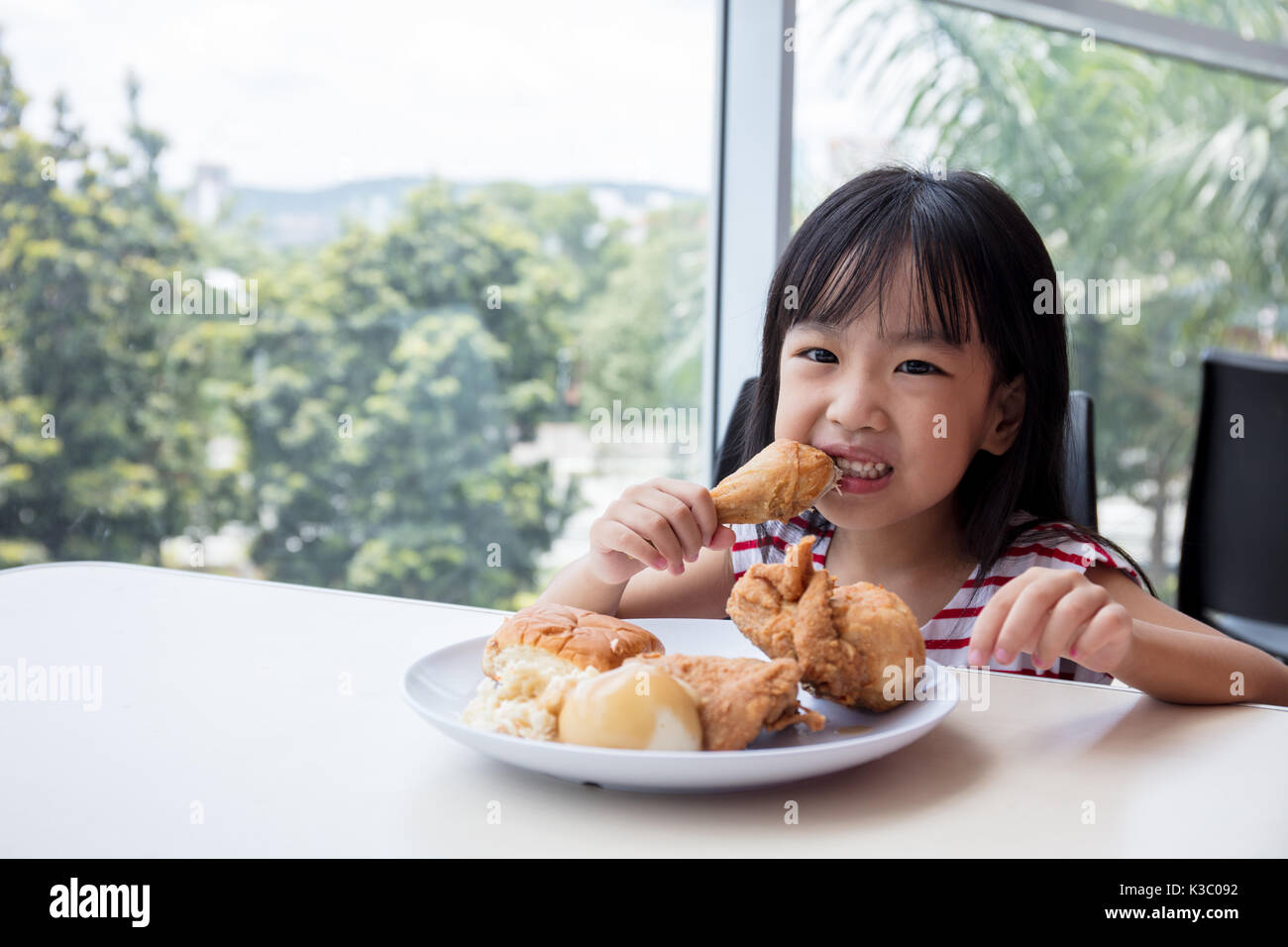 Asian Chinese little girl eating fried chicken at indoor restaurant ...