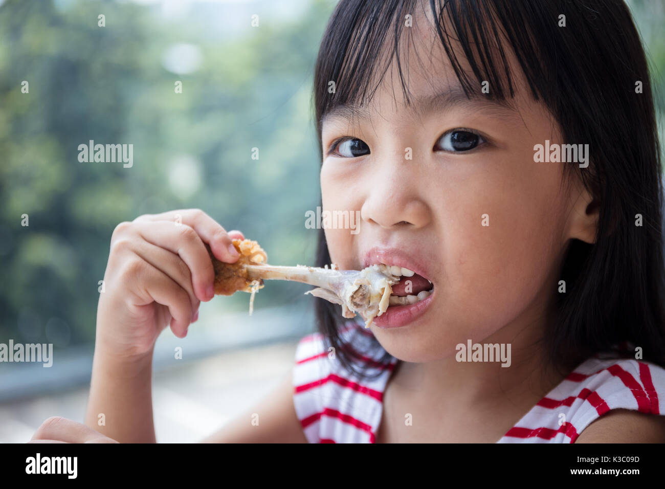 Asian Chinese little girl eating fried chicken at indoor restaurant ...