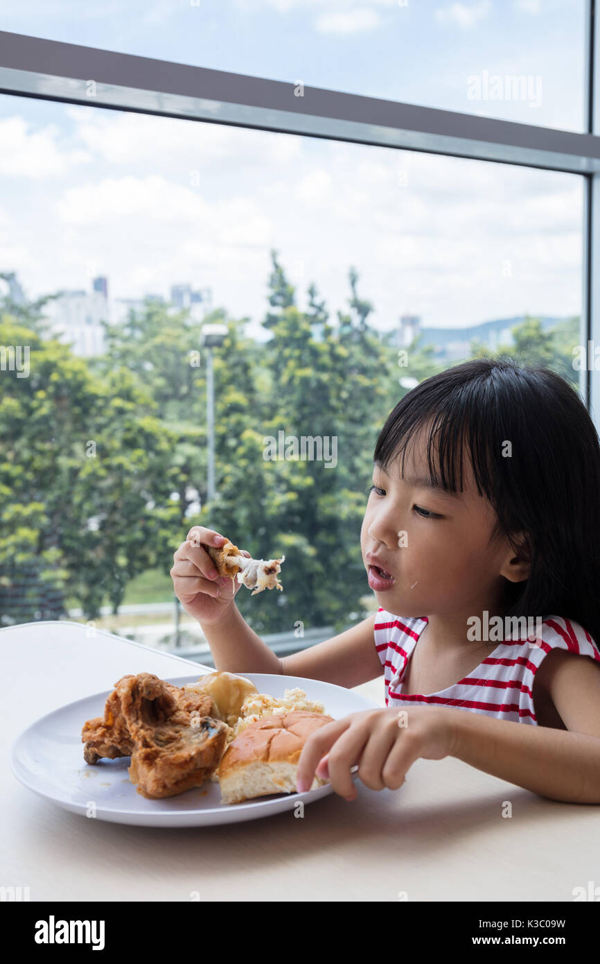 Asian Chinese little girl eating fried chicken at indoor restaurant ...