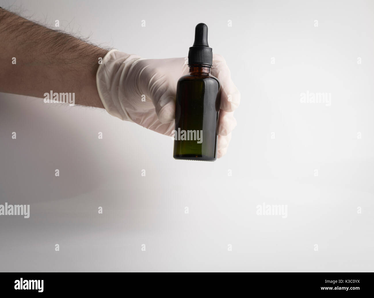 Isolated hand holding a medical brown drop bottle over a white ...