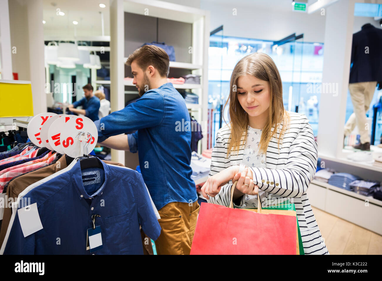 A photo of young people doing shopping. The man is browsing clothes and ...