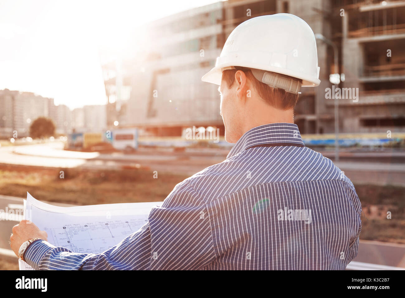 Architect in helmet with blueprints looks at camera in a building site ...