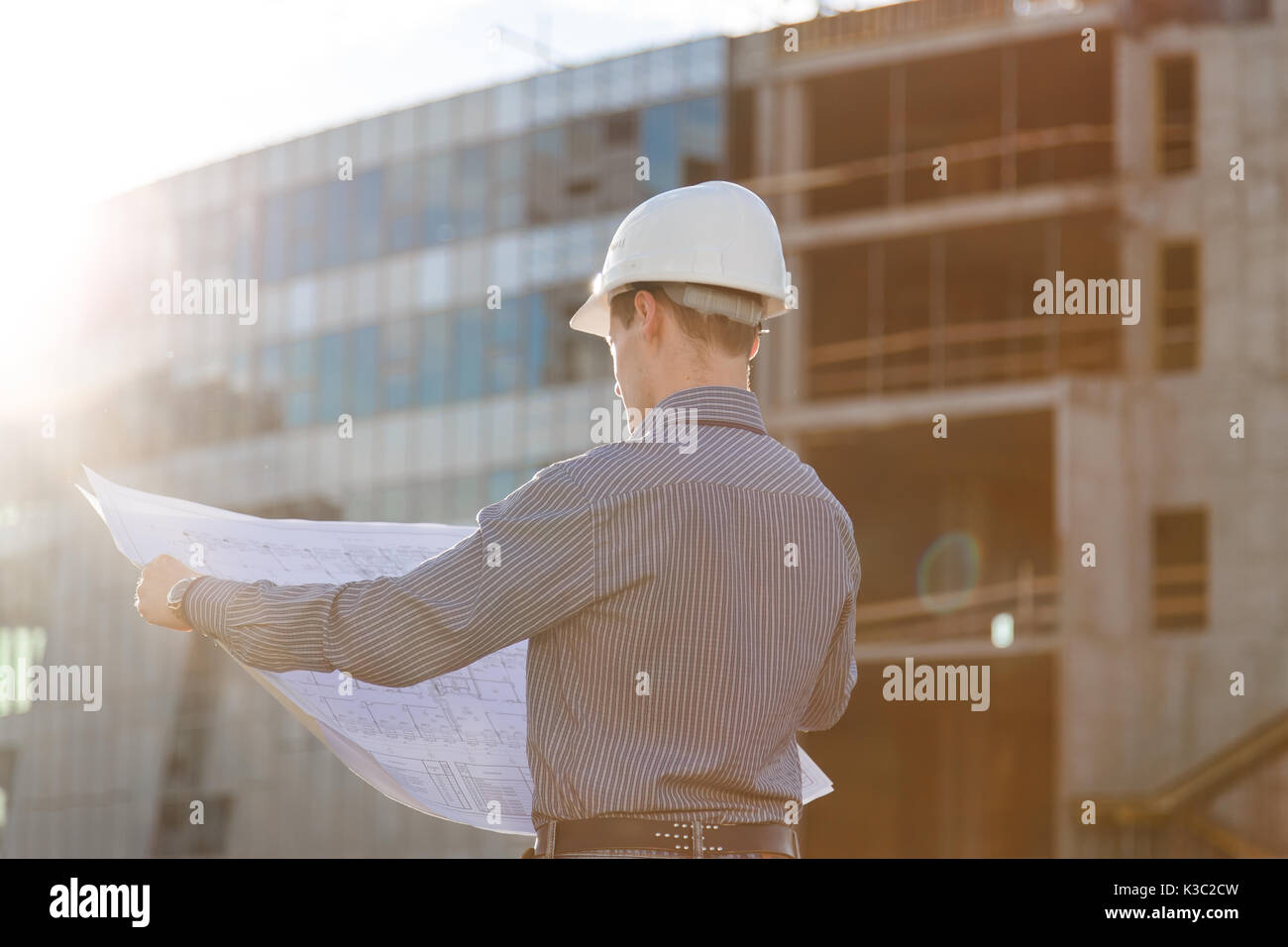 Architect in helmet with blueprints looks at camera in a building site ...