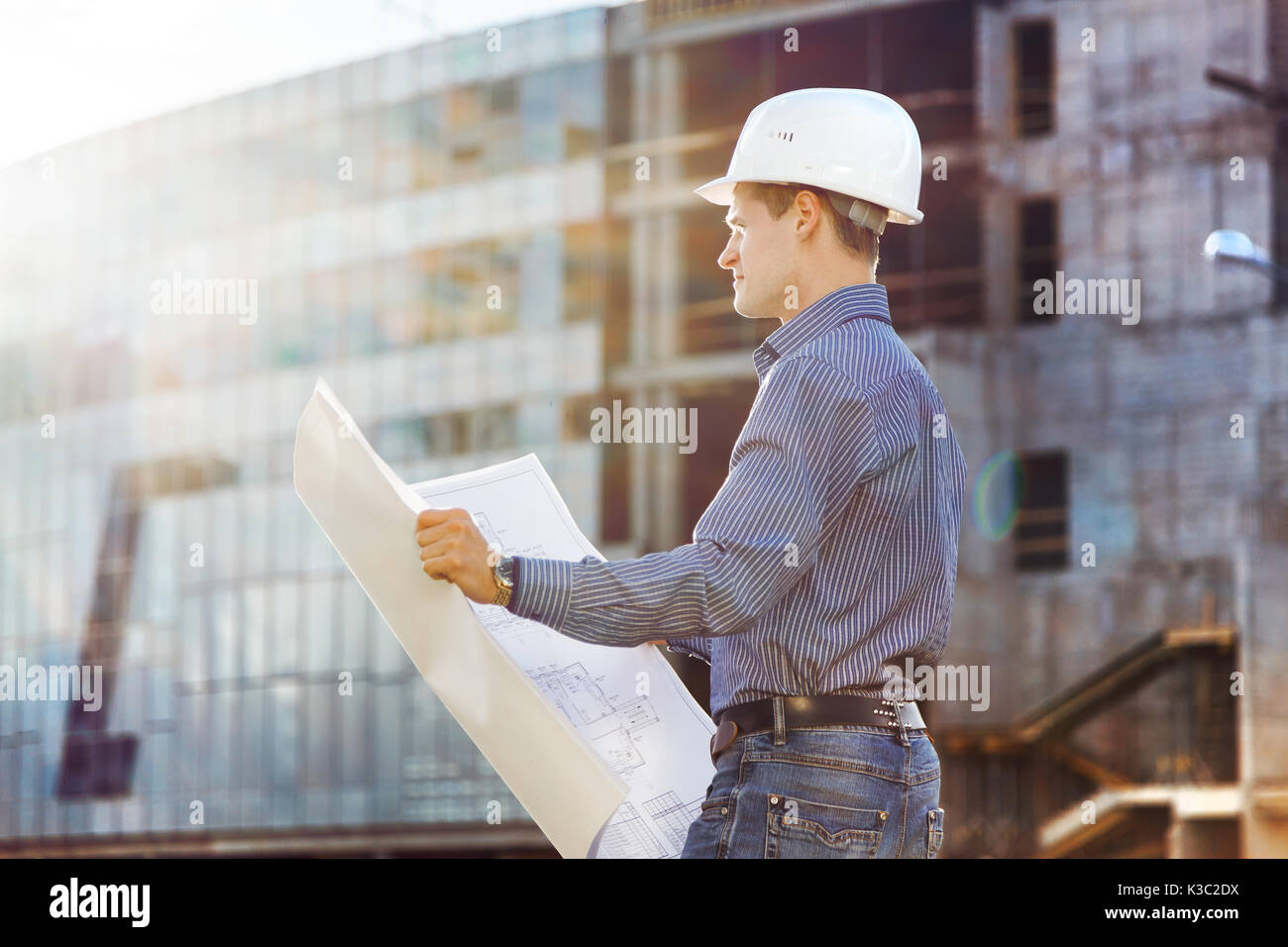 Architect in helmet with blueprints looks at camera in a building site ...