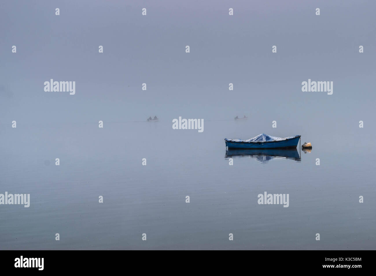 Boat on calm lake water in a foggy morning with other fishing boats in ...