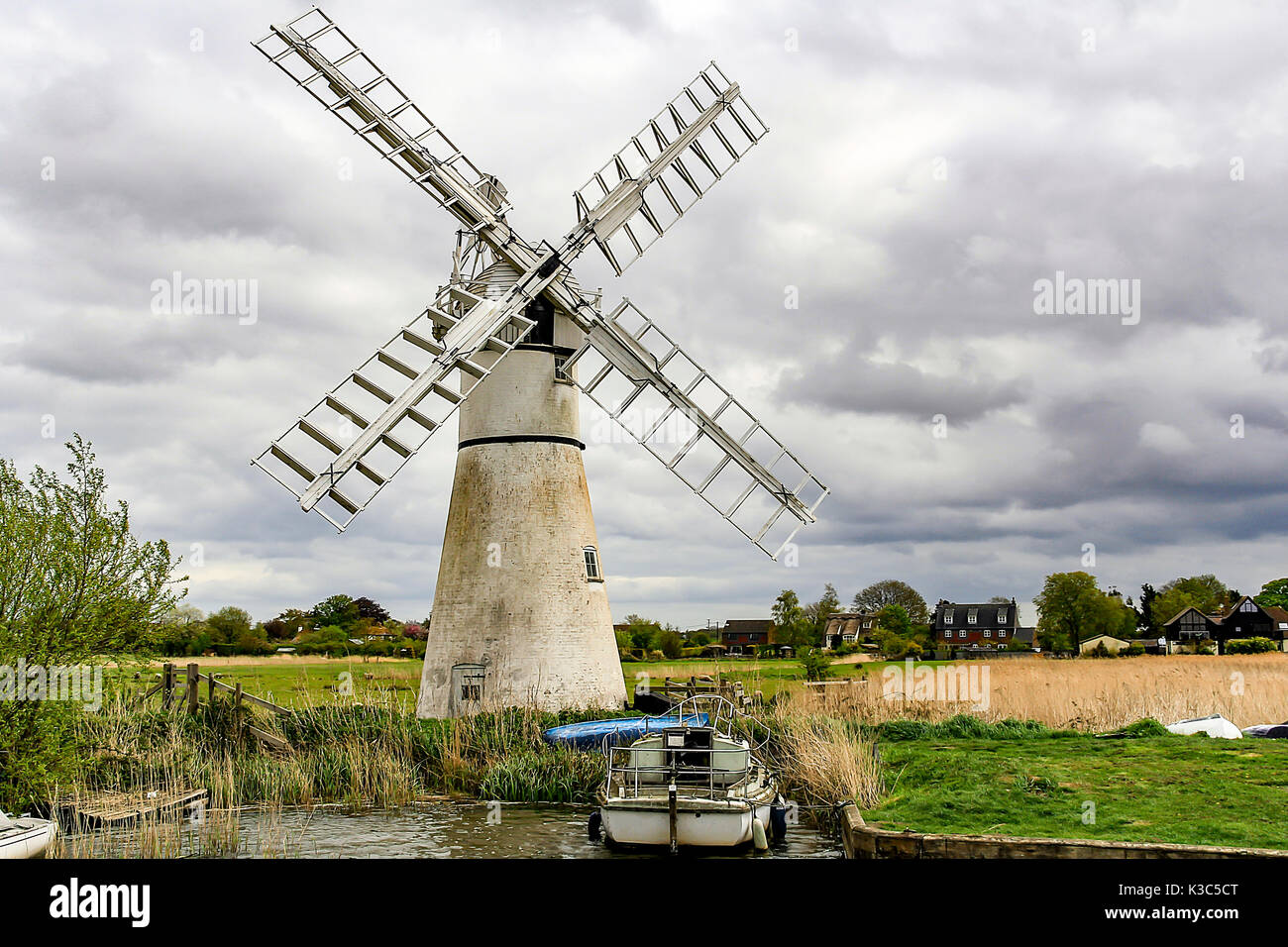 Windmill on the Norfolk Broads with a small boat moored alongside. The ...