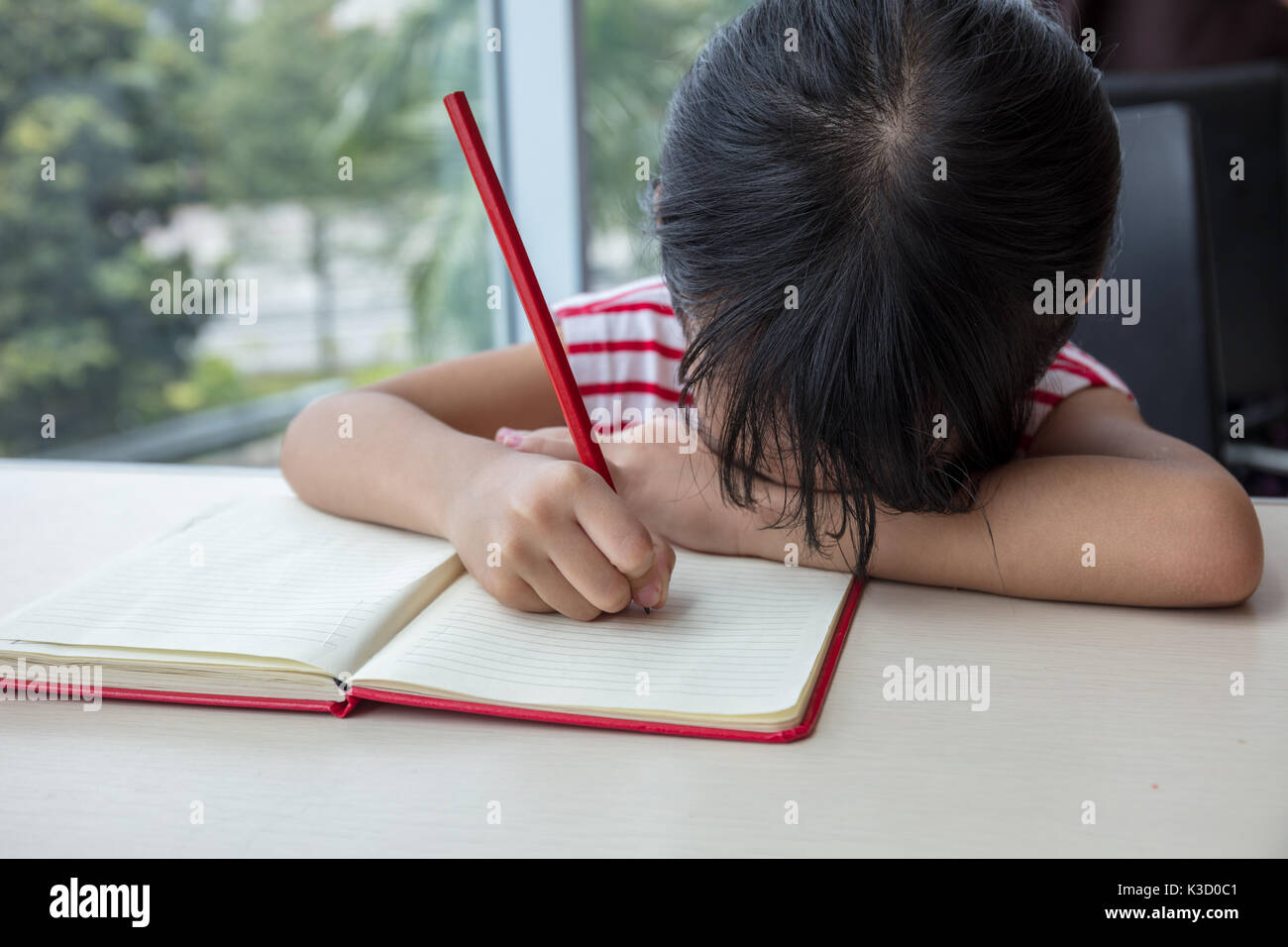 Boring asian little Chinese girl writing homework at home Stock Photo ...