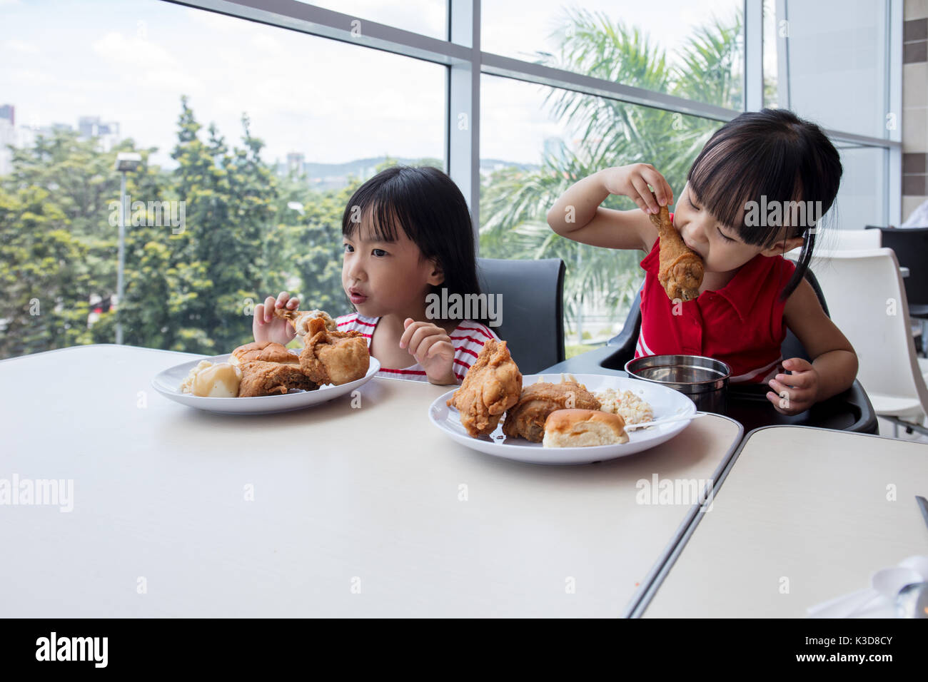 Asian Chinese little girls eating fried chicken at indoor restaurant ...