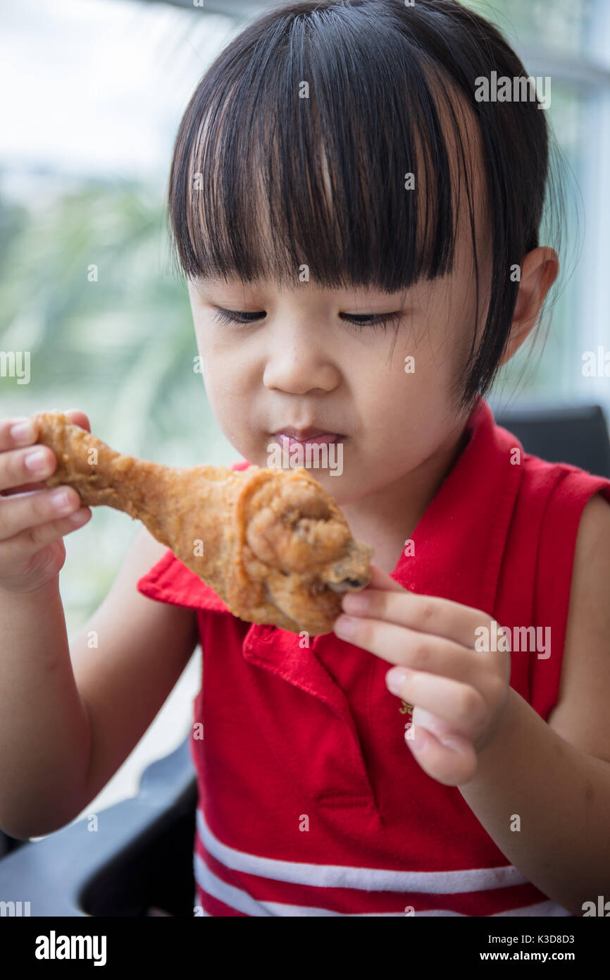 Asian Chinese little girl eating fried chicken at indoor restaurant ...