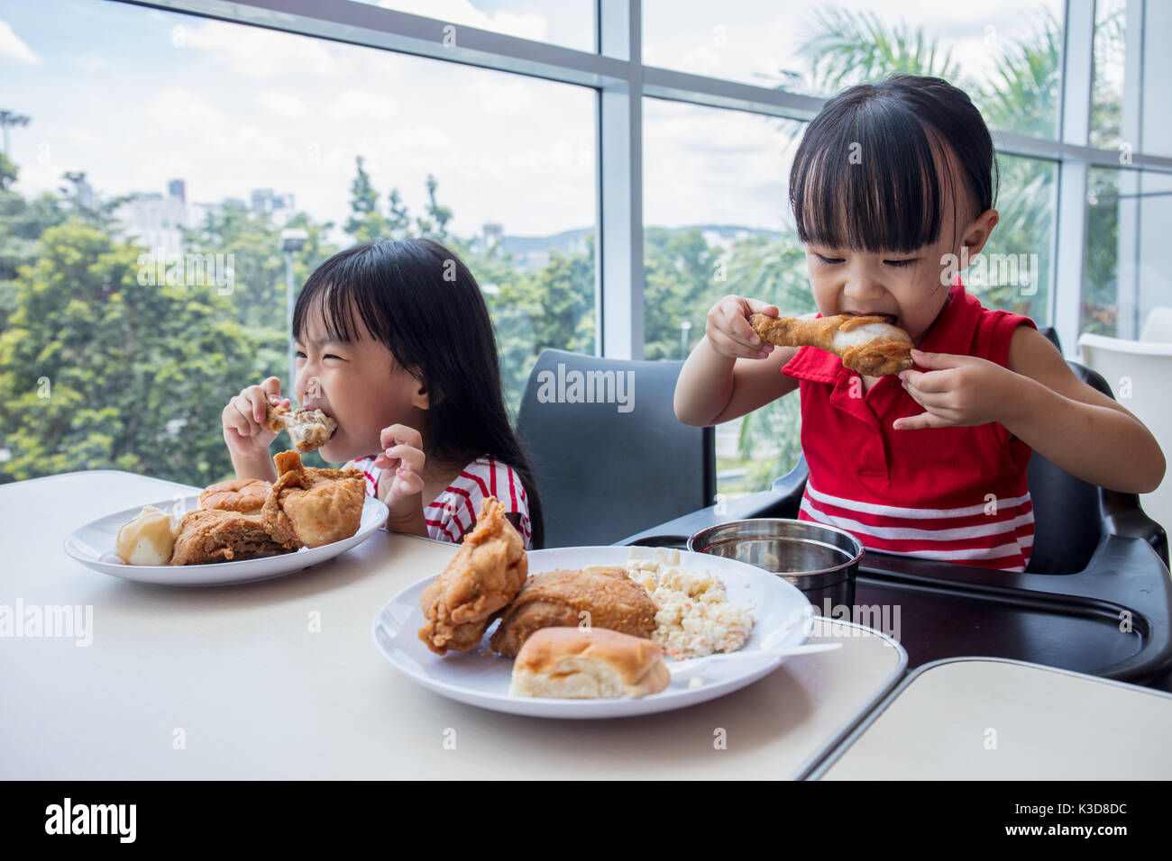 Asian Chinese little girls eating fried chicken at indoor restaurant ...