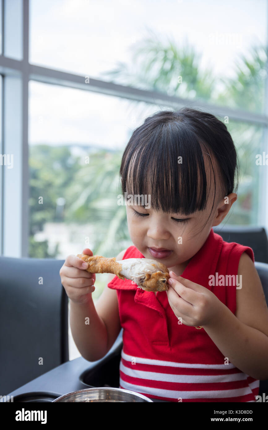 Asian Chinese little girl eating fried chicken at indoor restaurant ...