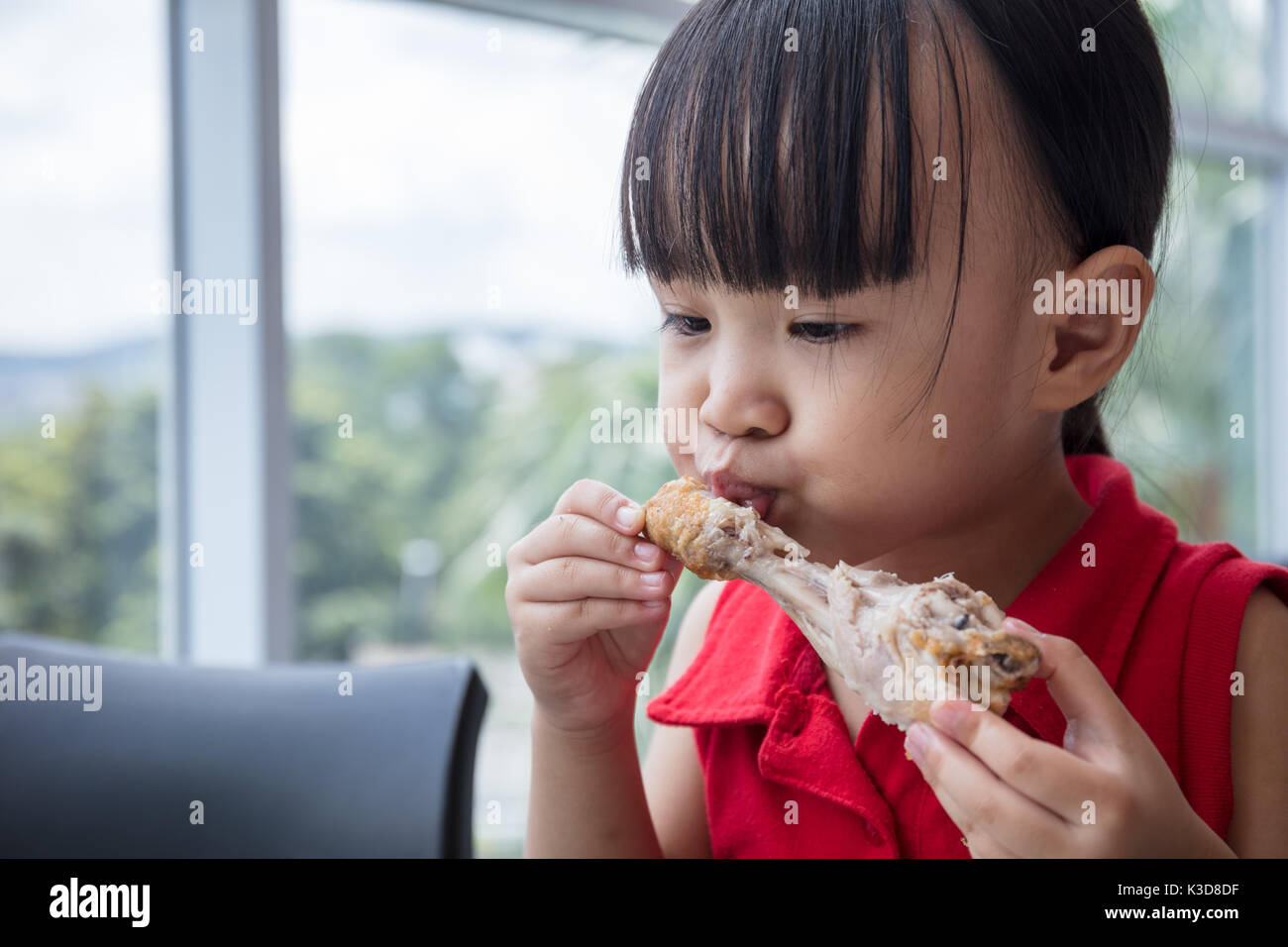 Asian Chinese little girl eating fried chicken at indoor restaurant ...